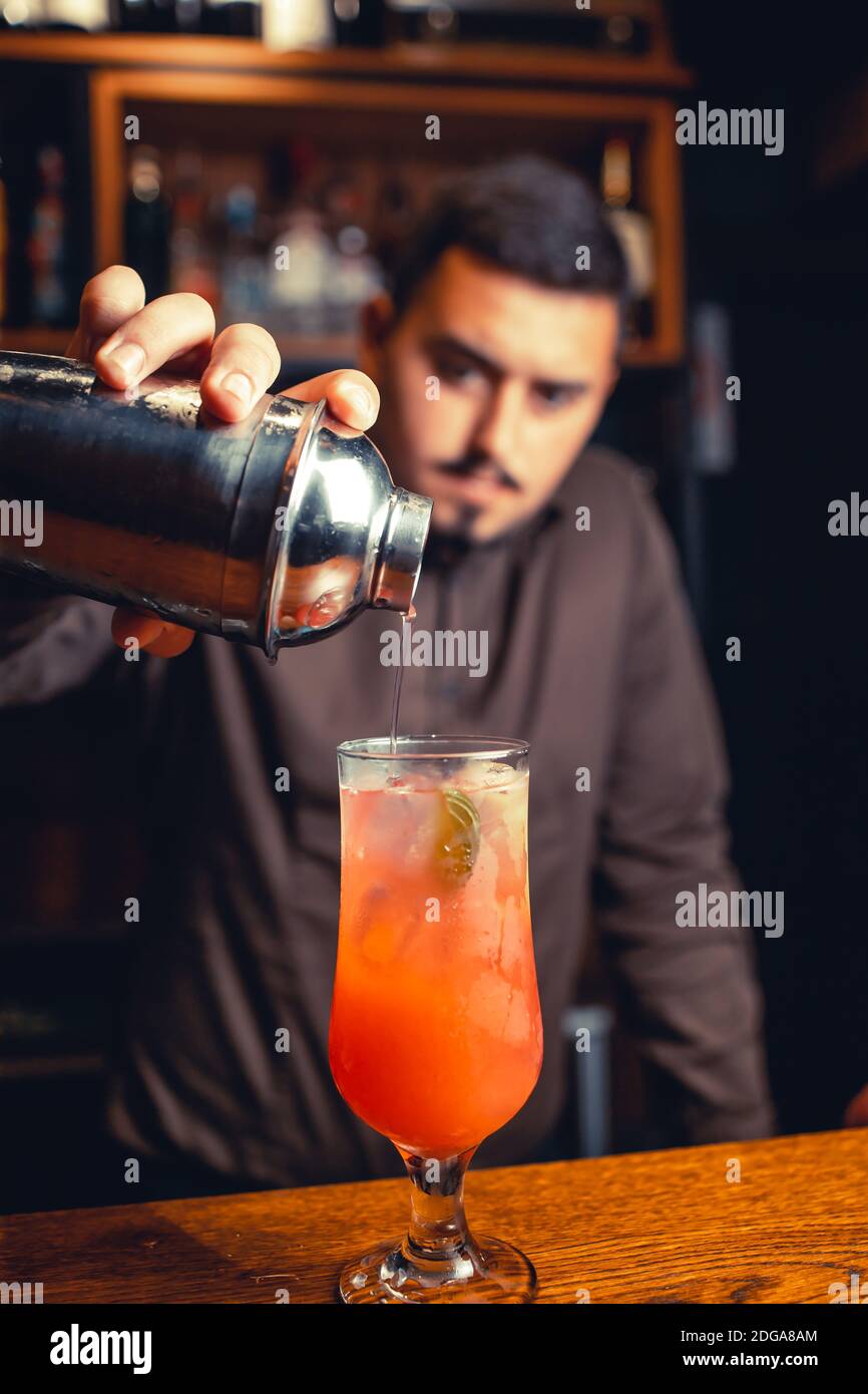 Portrait of elegant, young bartender behind the bar pouring red ...