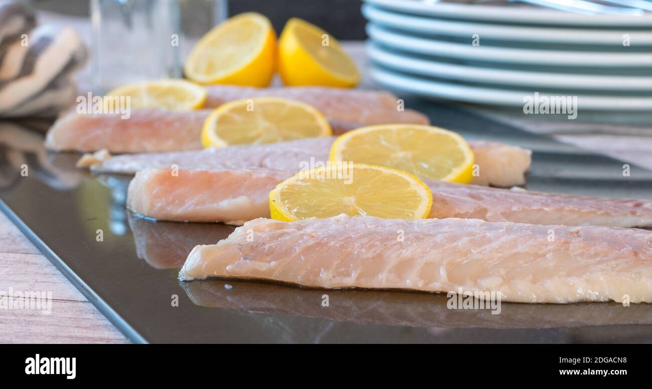 raw and uncooked redfish fillet on dark cutting board with lemon slices ...