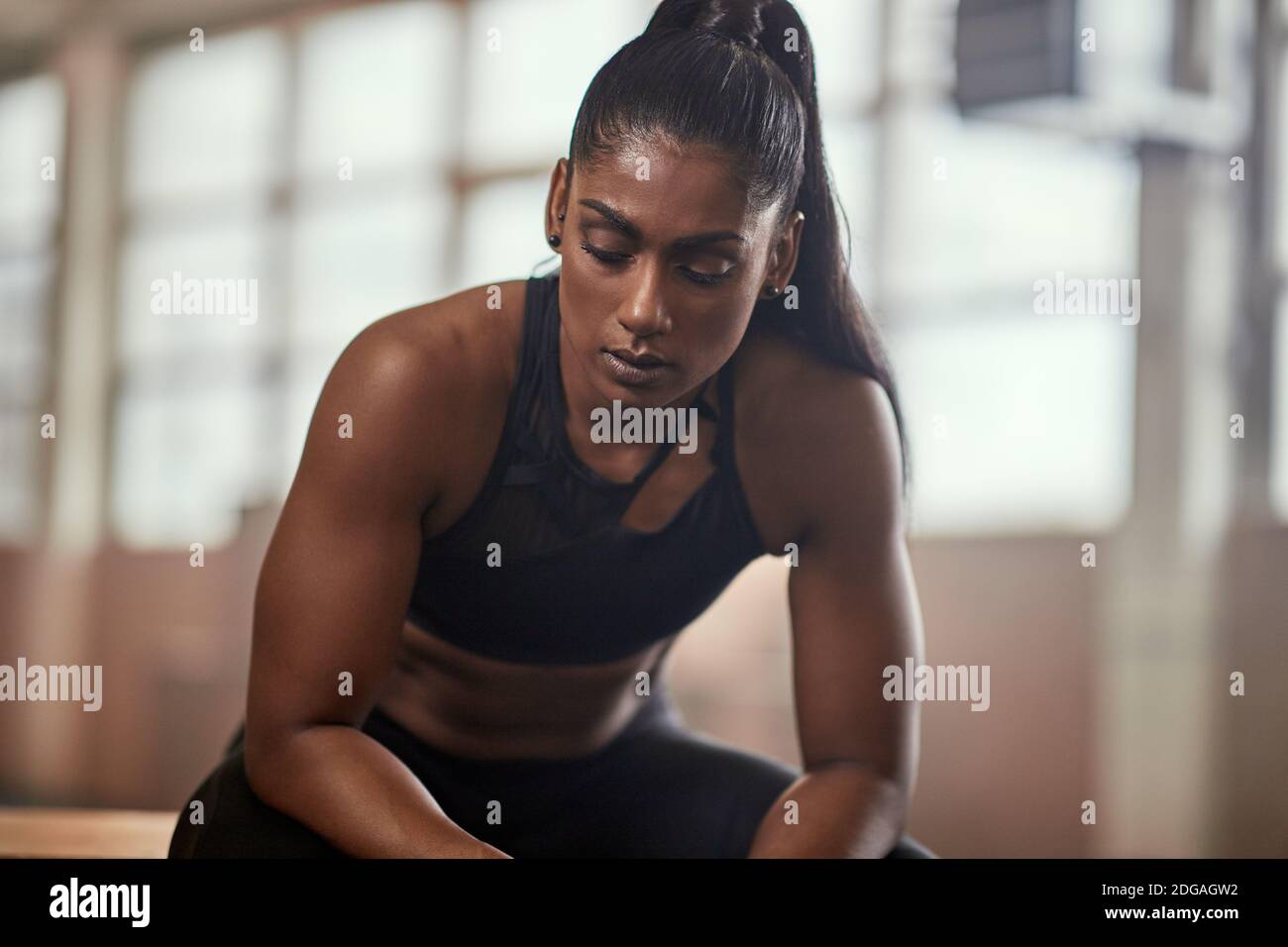 Muscular ethnic sportswoman with ponytail breathing and resting during ...