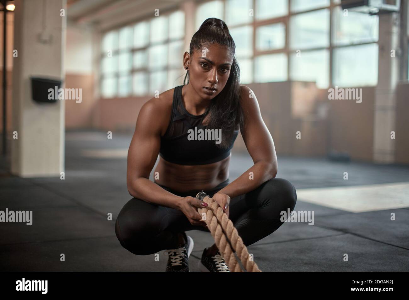 Powerful ethnic female athlete with rope sitting on haunches and ...