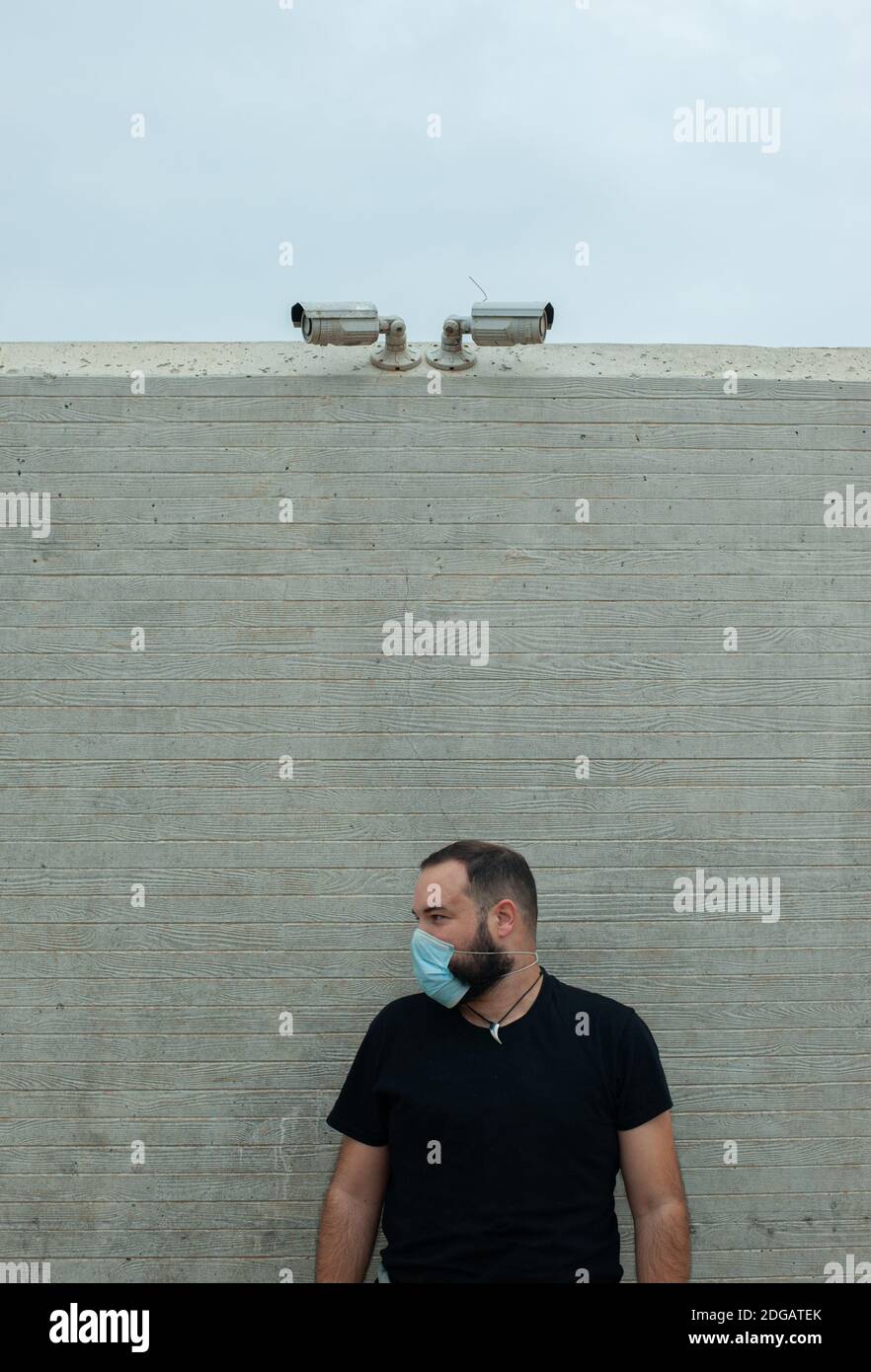 Man wearing surgical mask standing under security cameras. New normal ...