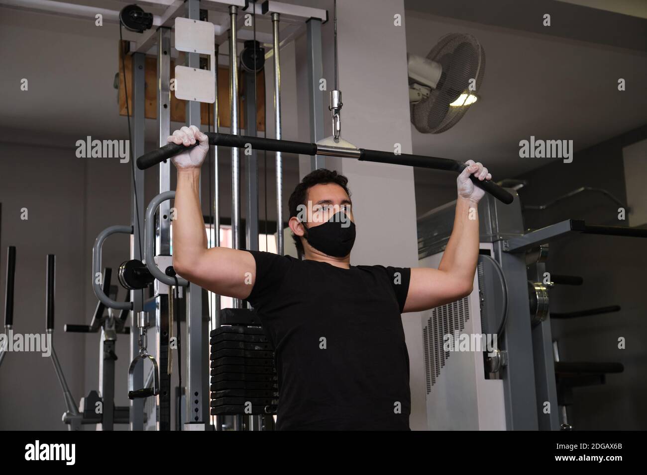 Sporty man wearing protective face mask exercising with lat pulldown ...