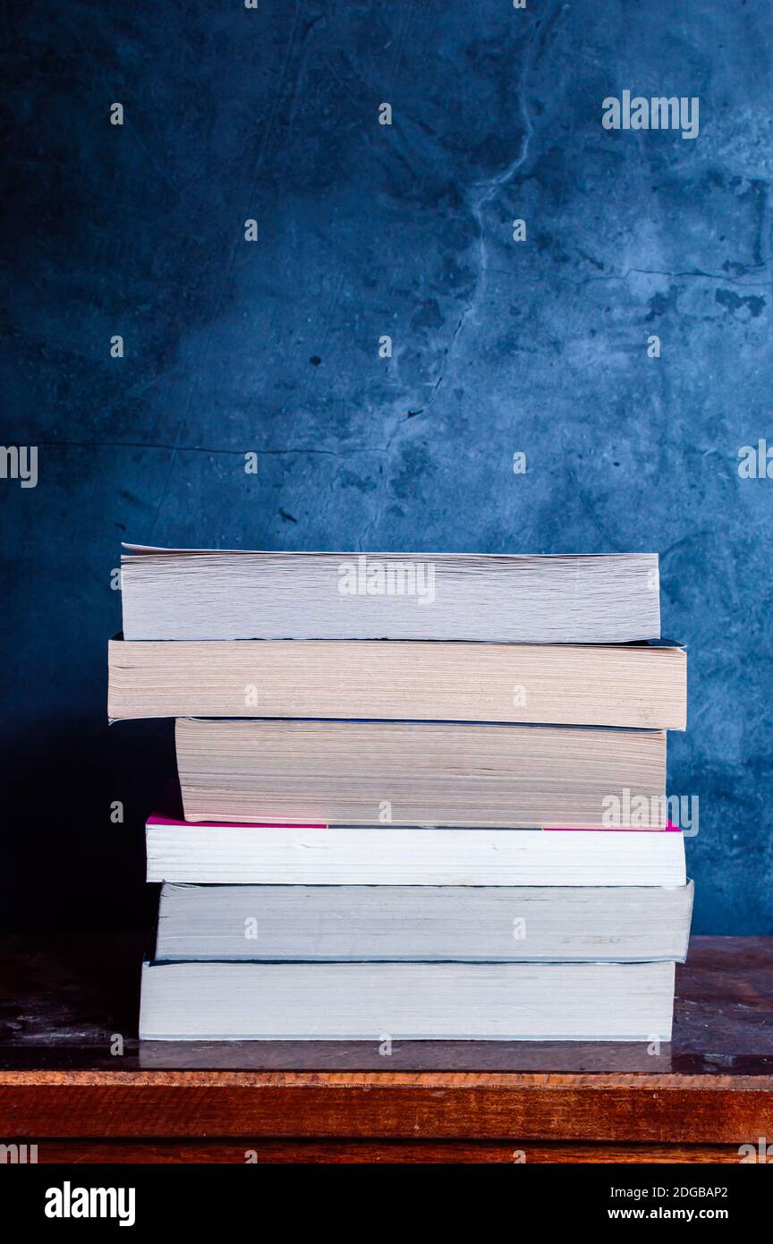 A stack of books sitting on a dusty table against a gray background ...