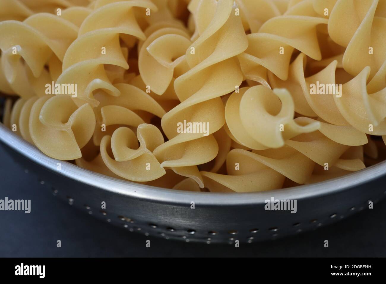 A closeup of the raw fresh fusilli pasta in a steel colander on a gray ...