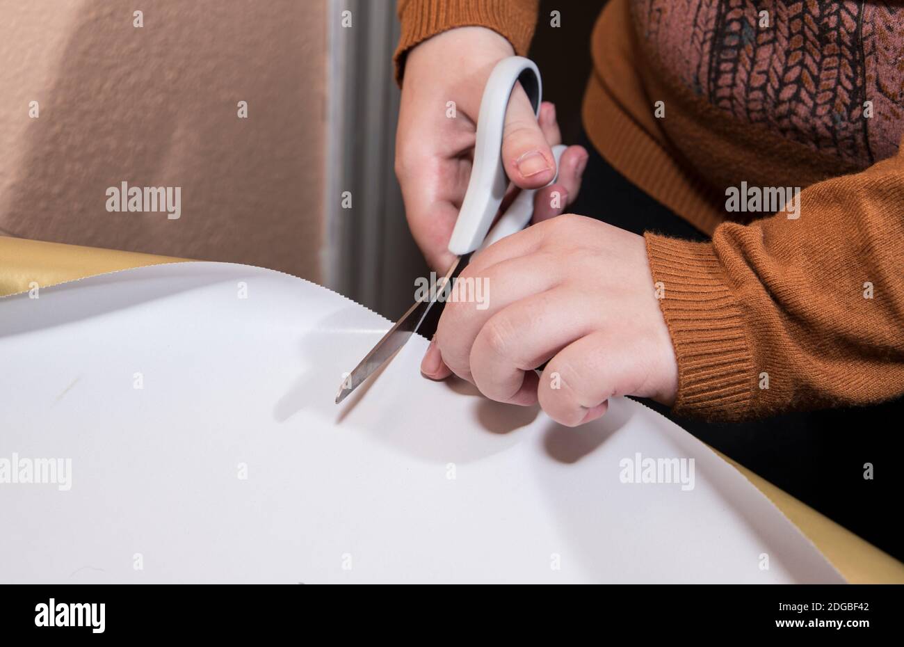 Young girl cuts golden colored wrapping paper with white scissors on a ...