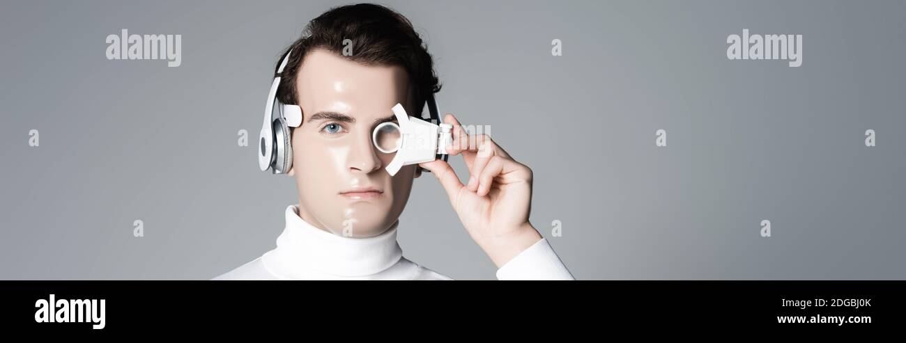 Cyborg in headphones looking at camera while holding digital eye lens ...