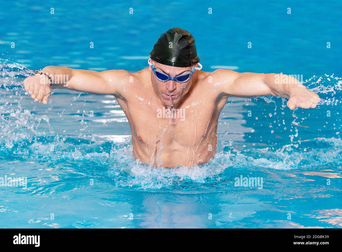 Muscular swimmer young man in black cap in swimming pool, performing ...