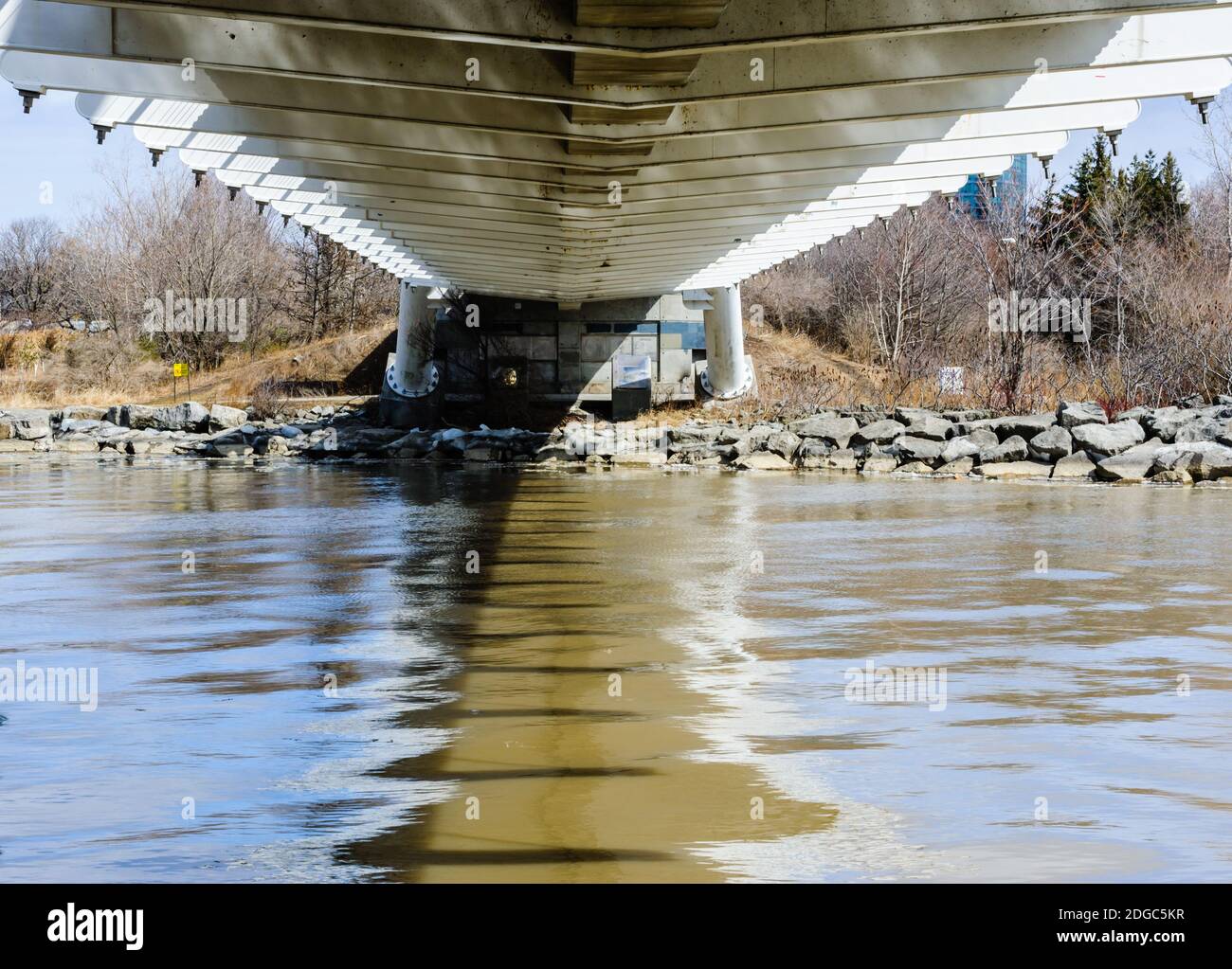 Underneath small metal bridge girders crossing muddy river, in Toronto ...