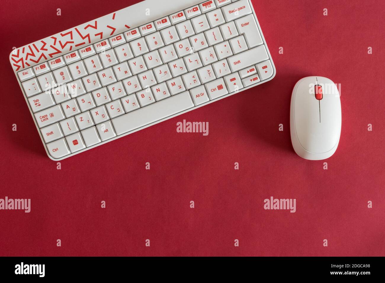 A flat lay of a modern white keyboard with a wireless mouse on a red ...