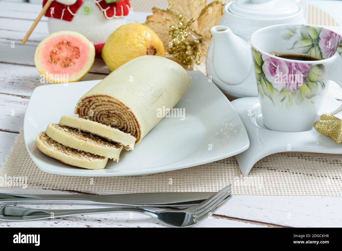 Bolo de rolo (roll cake) sliced next to cutlery, cup of coffee and ...