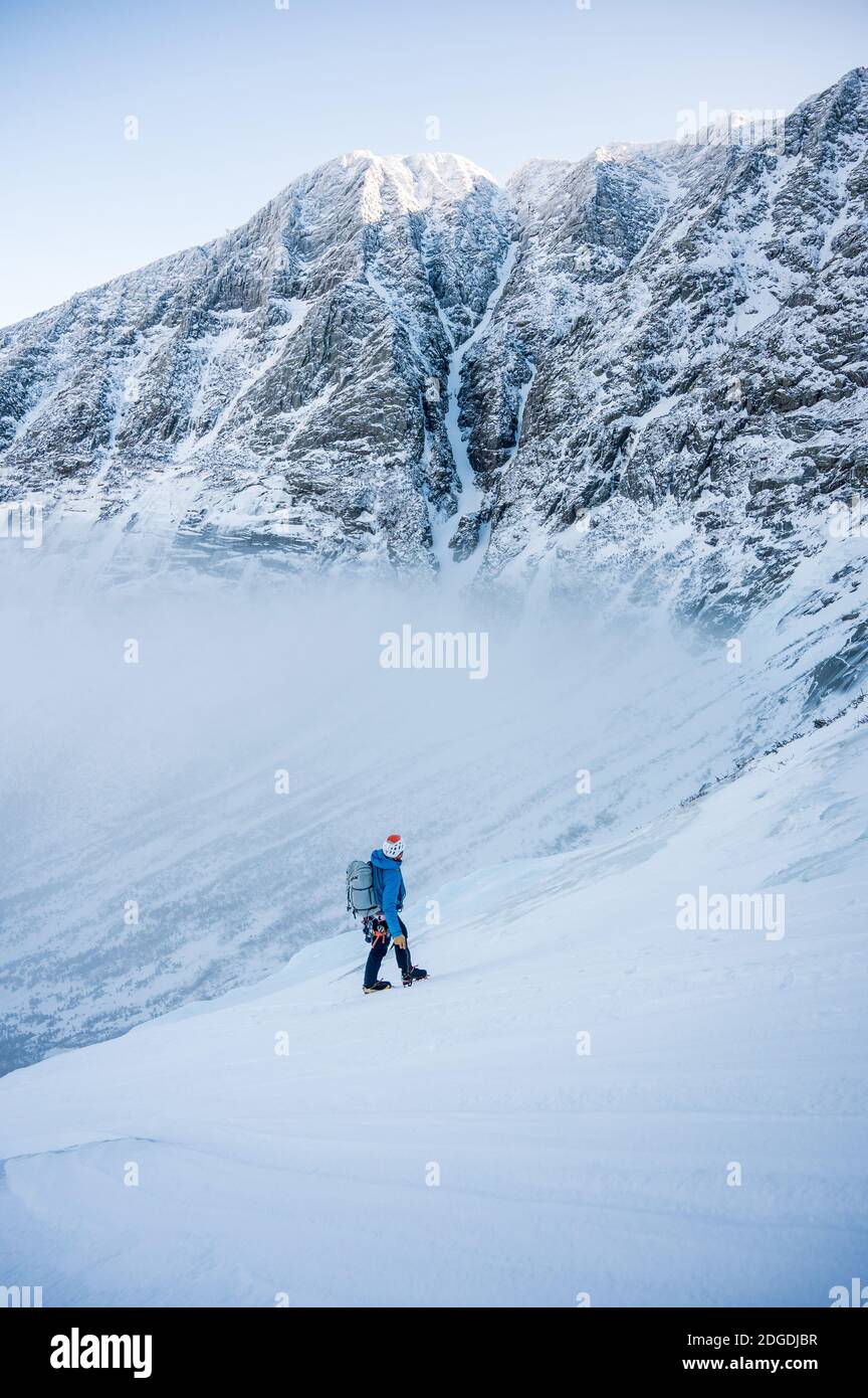 Male alpine climber ascends a steep section of snow, mountains behind ...