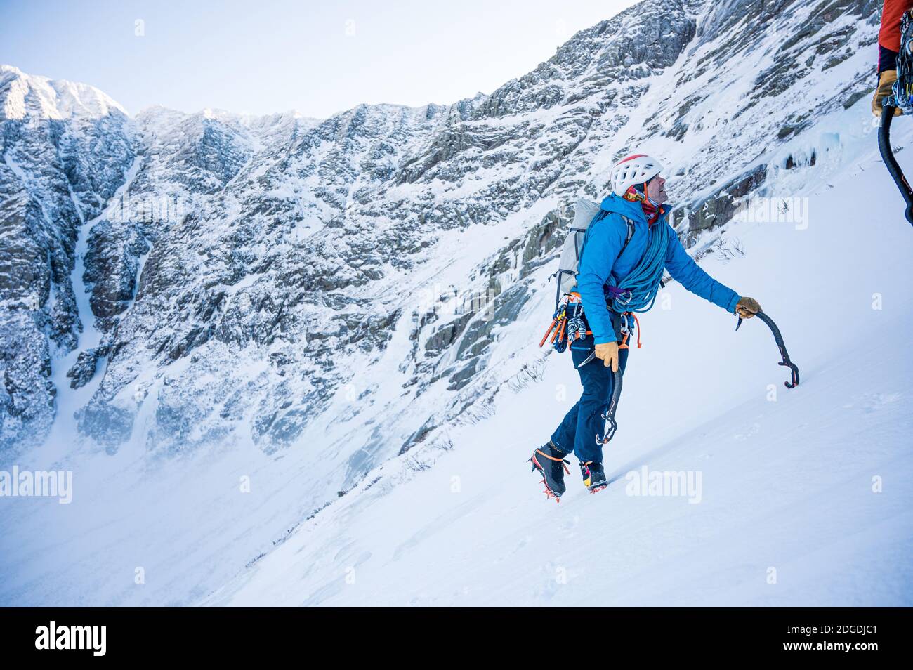 Male alpine climber ascends a steep section of snow, mountains behind ...