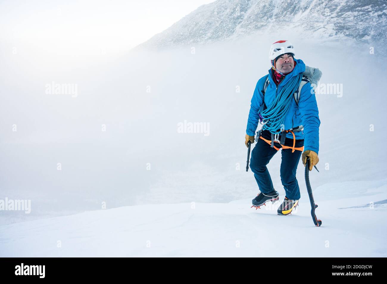 A male alpine climber ascends a steep section of snow with clouds ...
