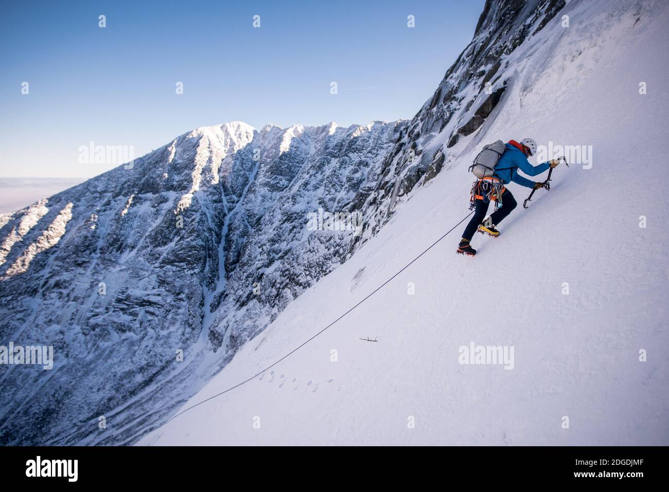 Alpine climber ascending steep snow with mountains behind Stock Photo ...