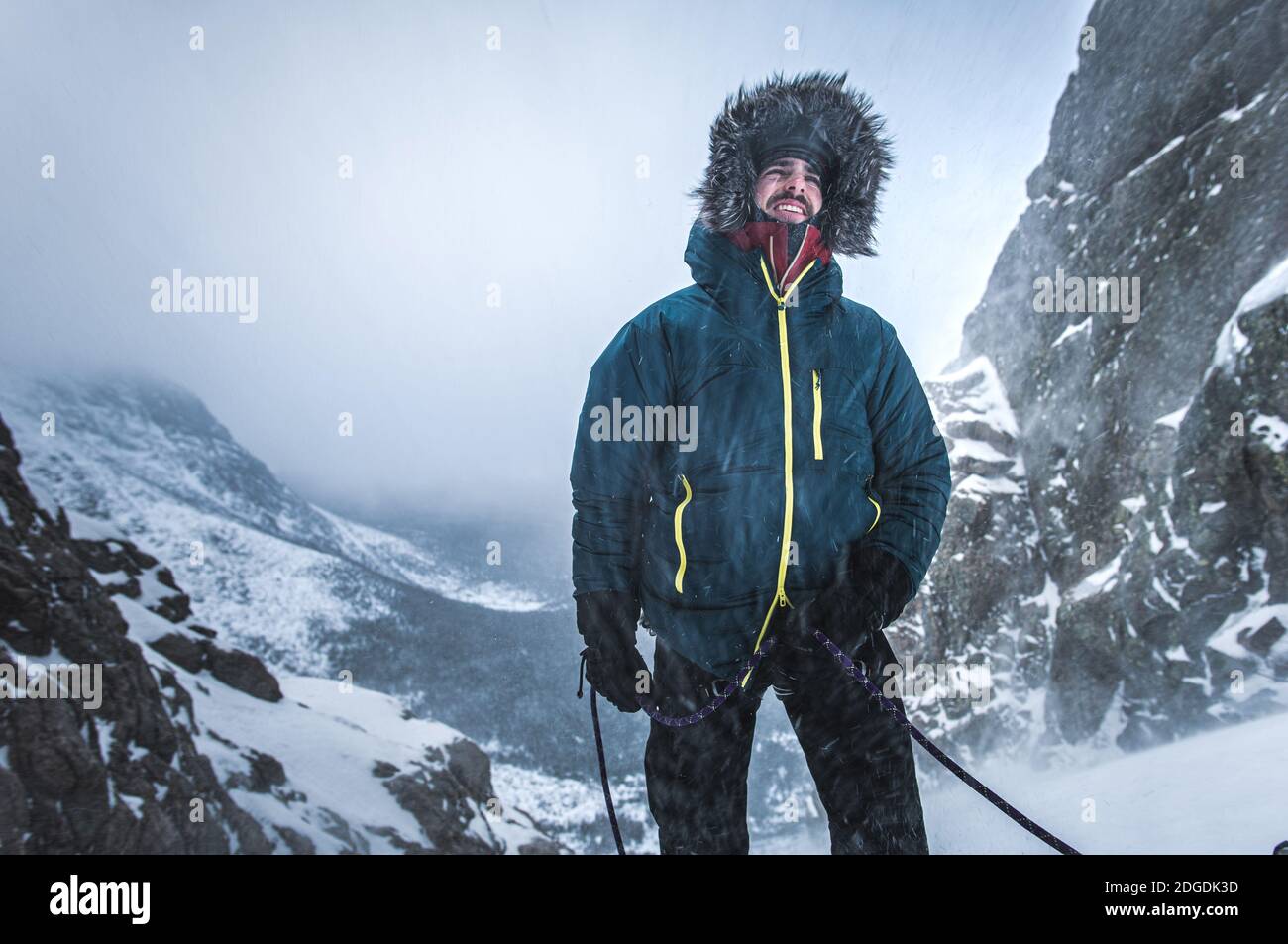 Male alpine climber belays his lead climber as snow blows in the cold ...