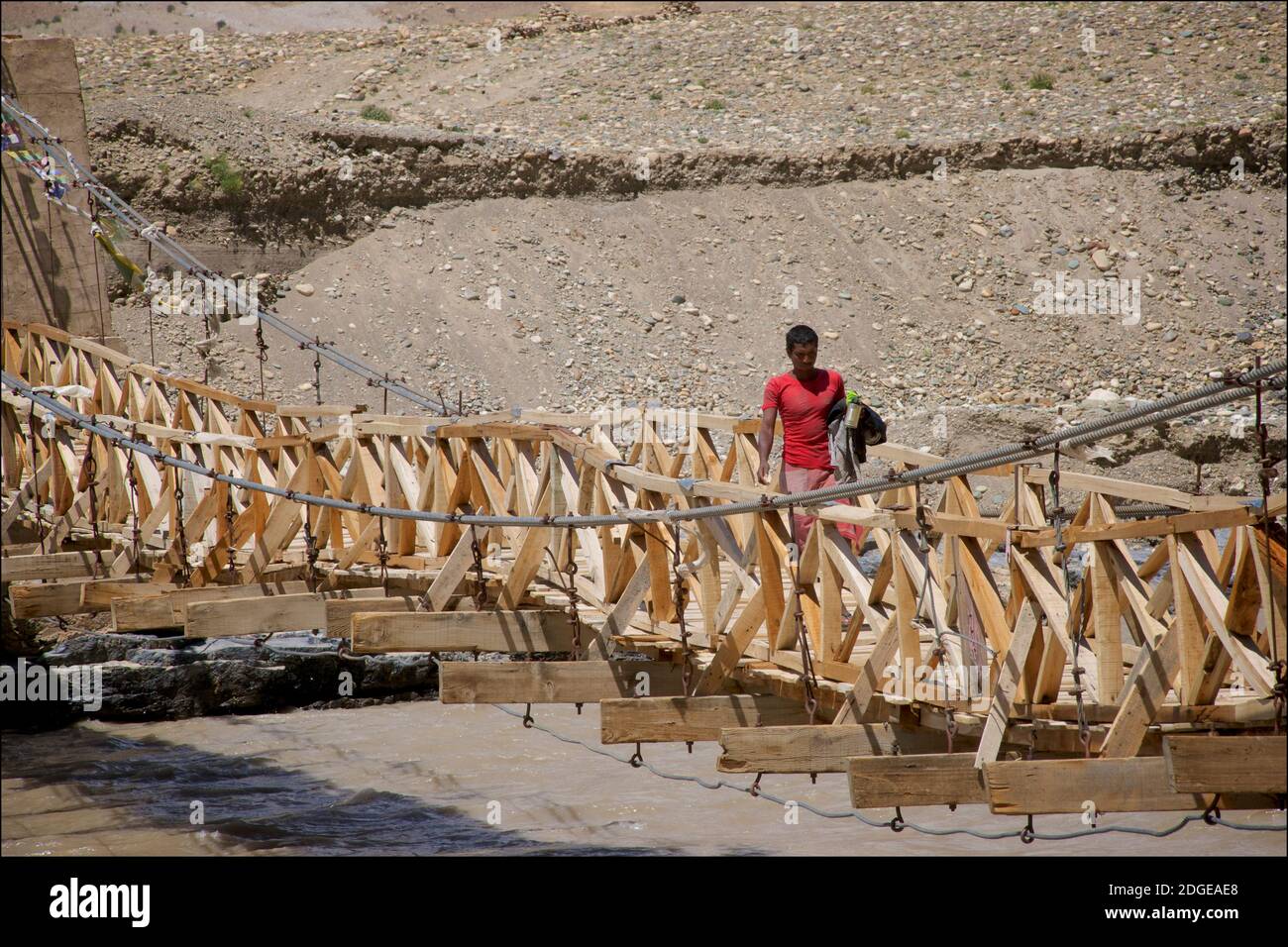 Man walking across a wooden suspension bridge over the Zanskar river ...
