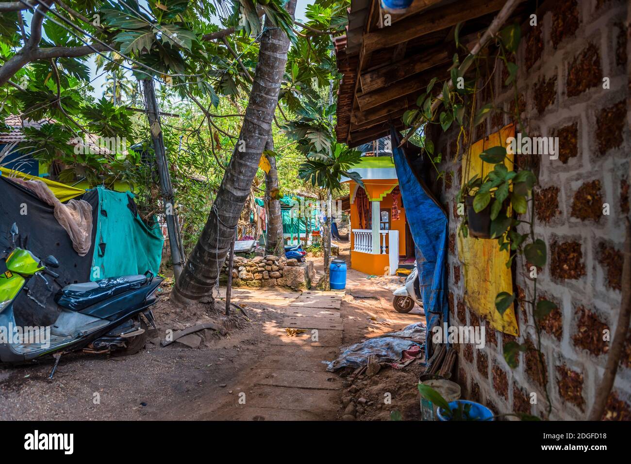 View of a narrow village street with motorcycles and palm trees in Goa ...