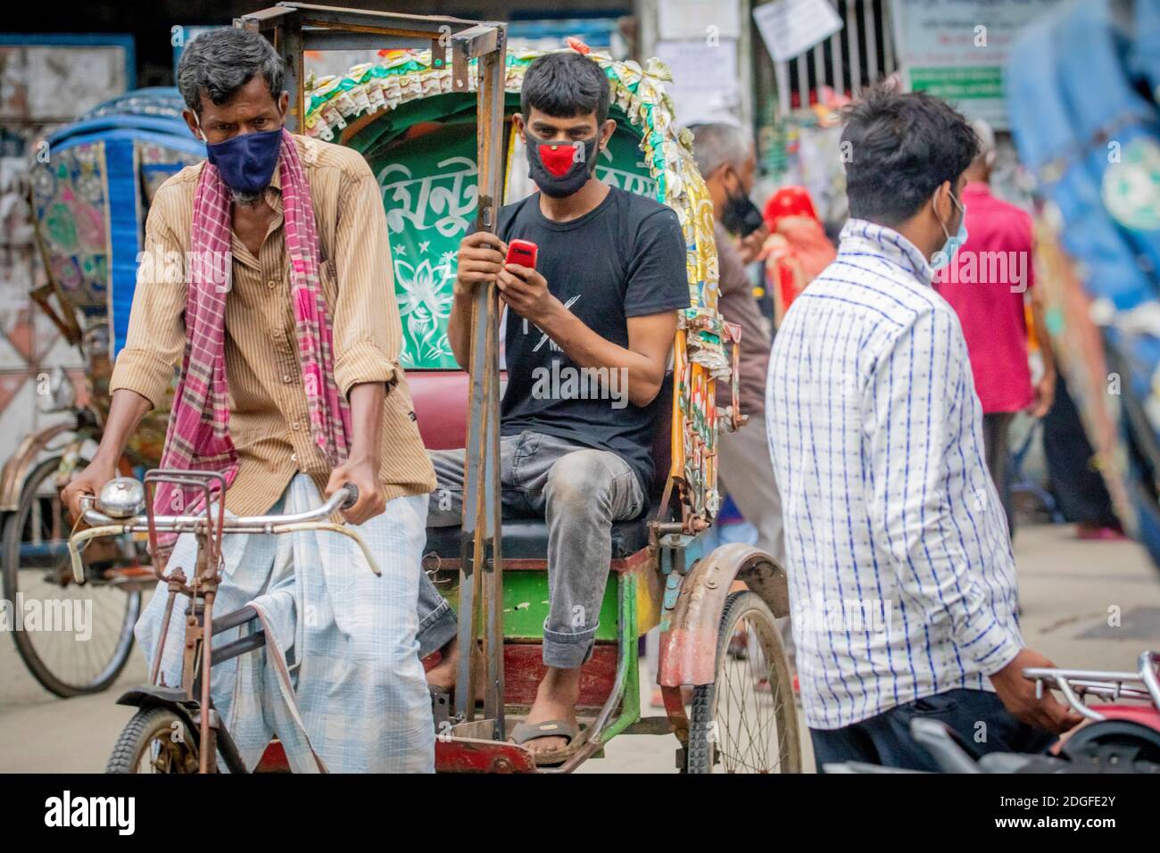A mask wearing passenger being pulled by a mask wearing rickshaw puller ...