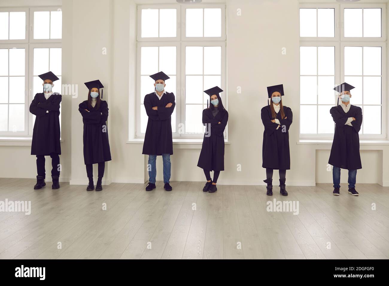 Students in graduation robes and face masks standing in university room ...