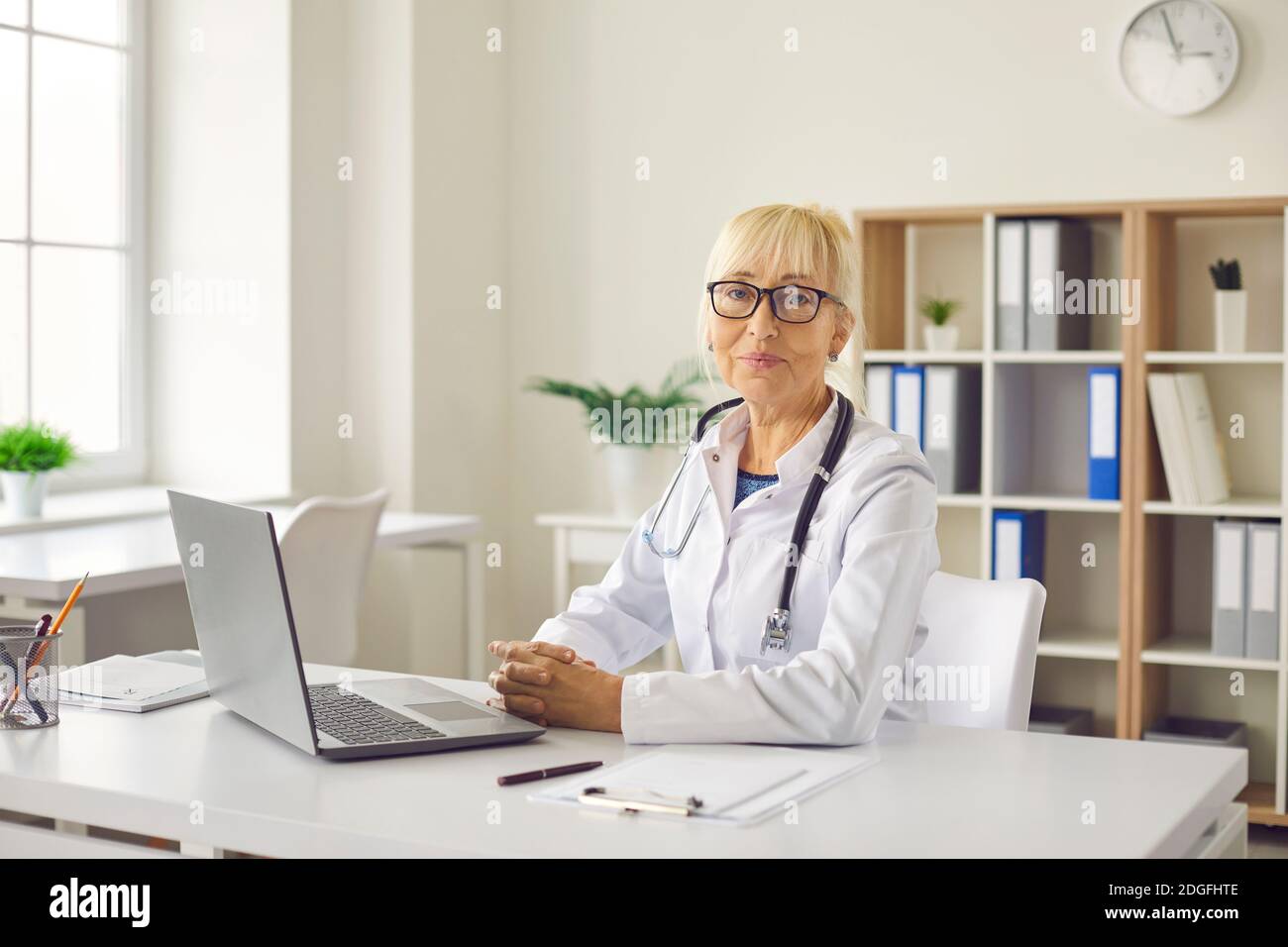 Positive senior professional woman doctor in uniform sitting with ...