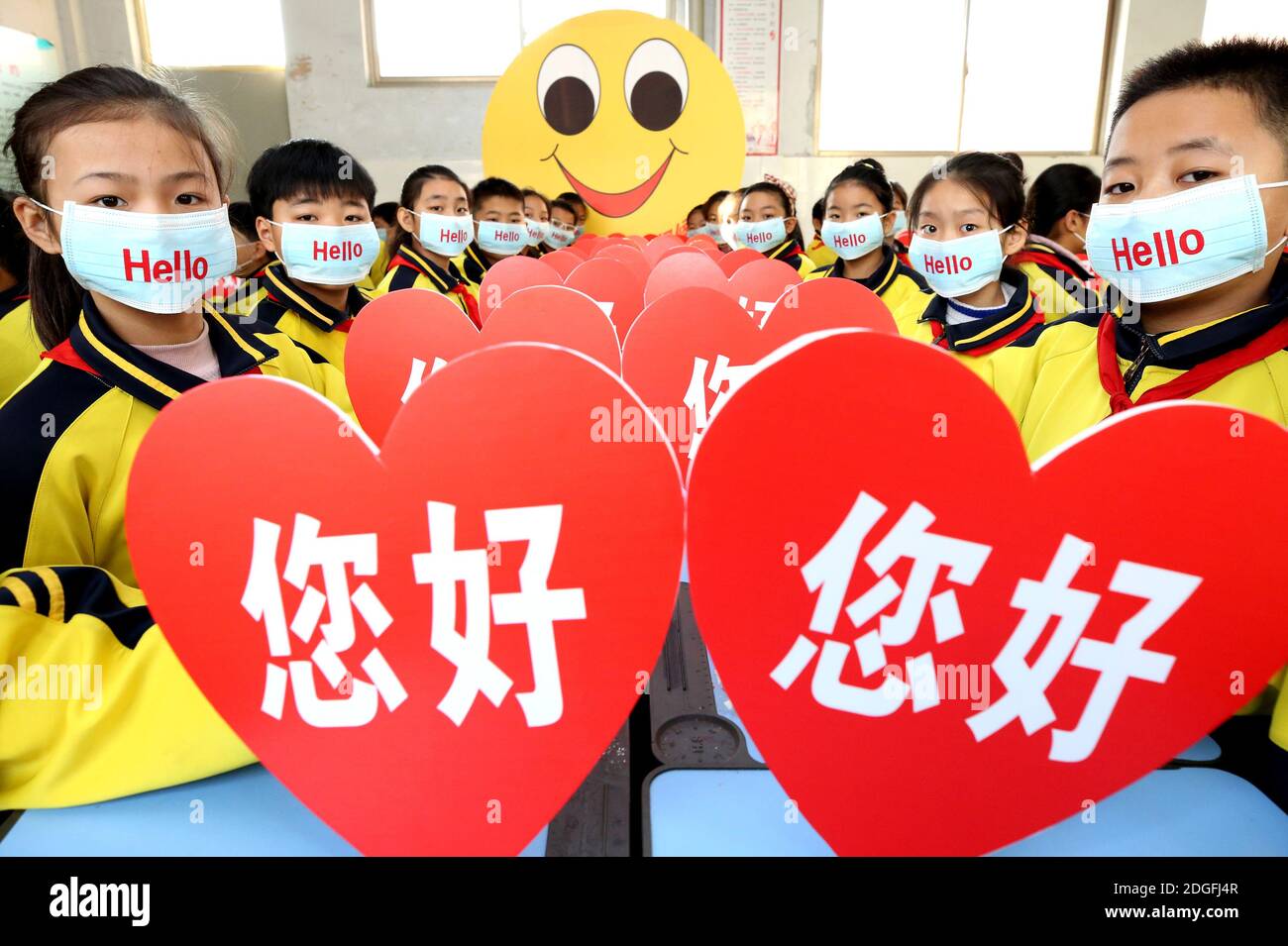 Pupils wear masks with Hello written on them and hold signs in their ...