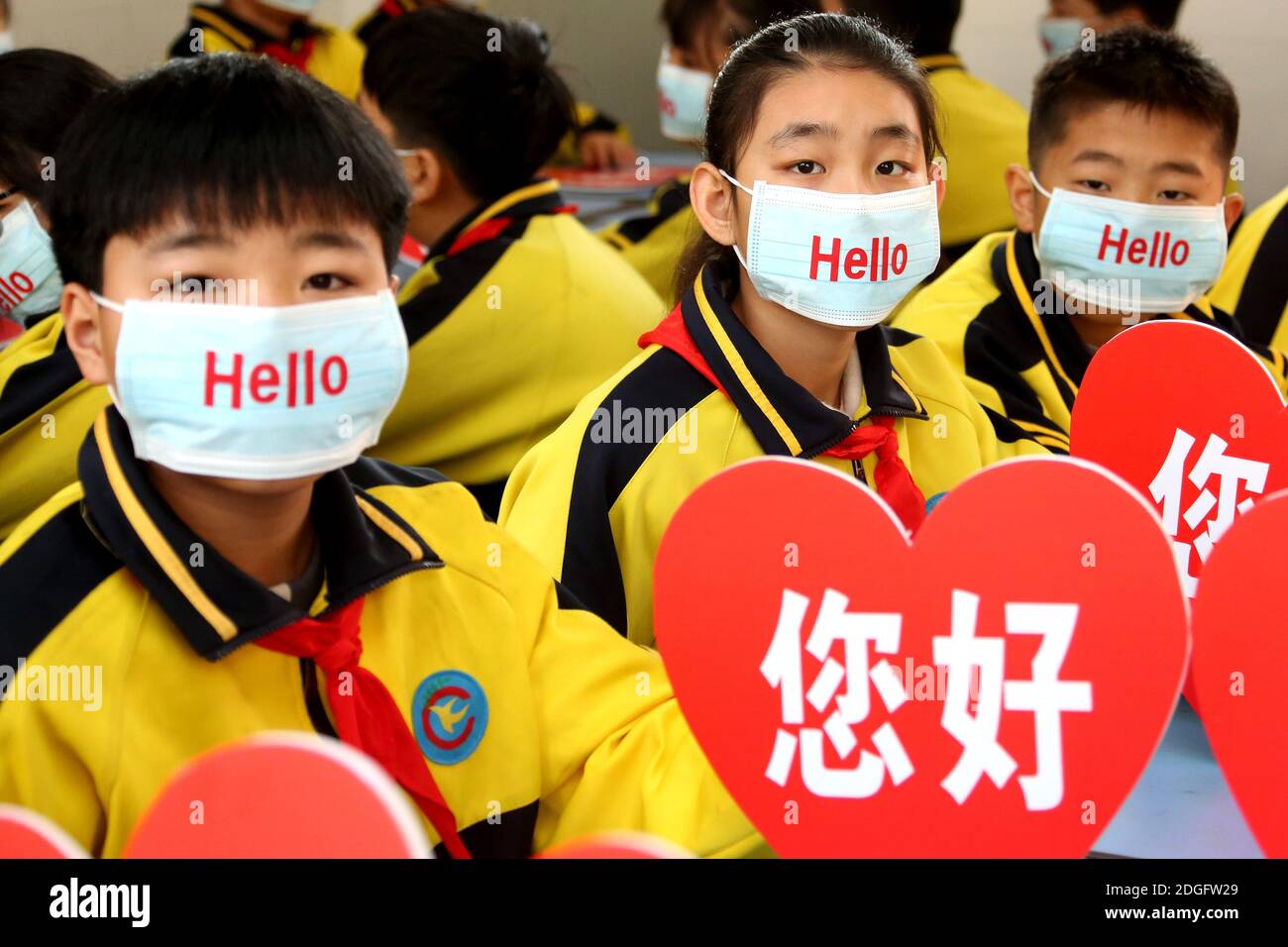 Pupils wear masks with Hello written on them and hold signs in their ...