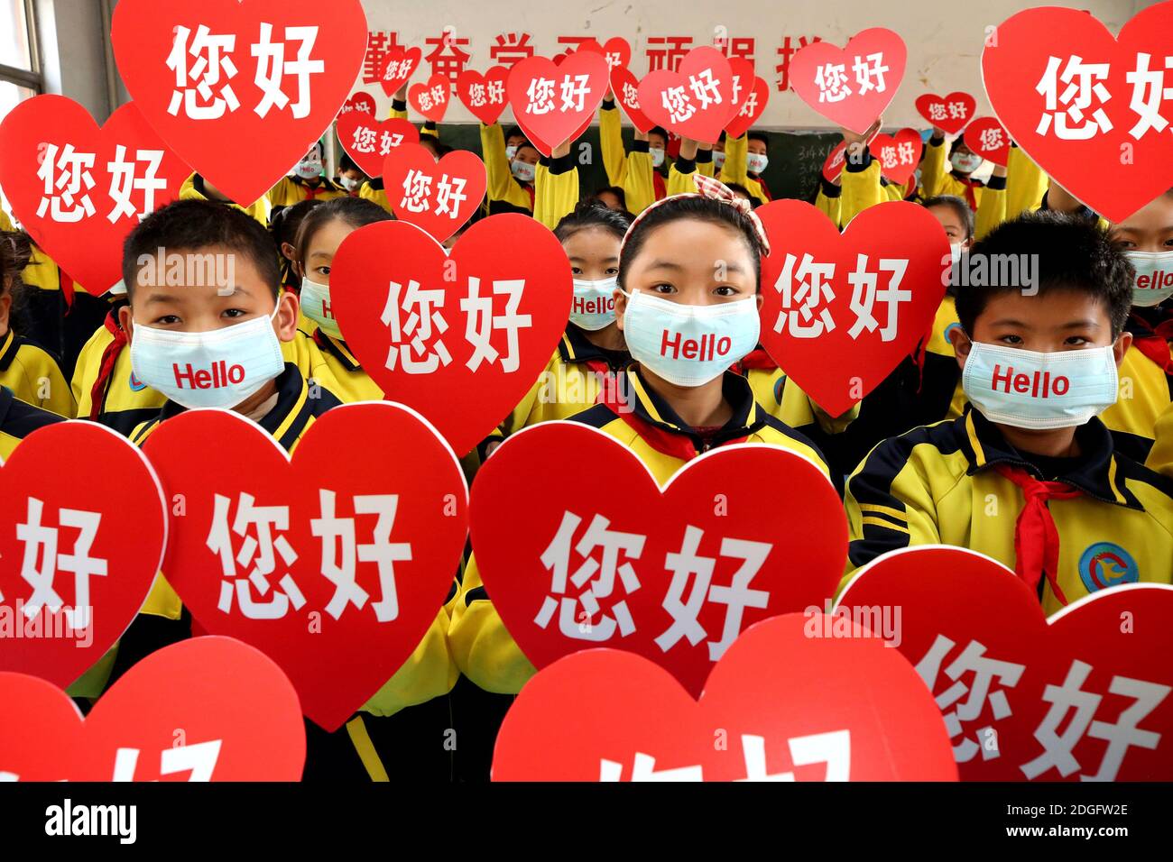 Pupils wear masks with Hello written on them and hold signs in their ...