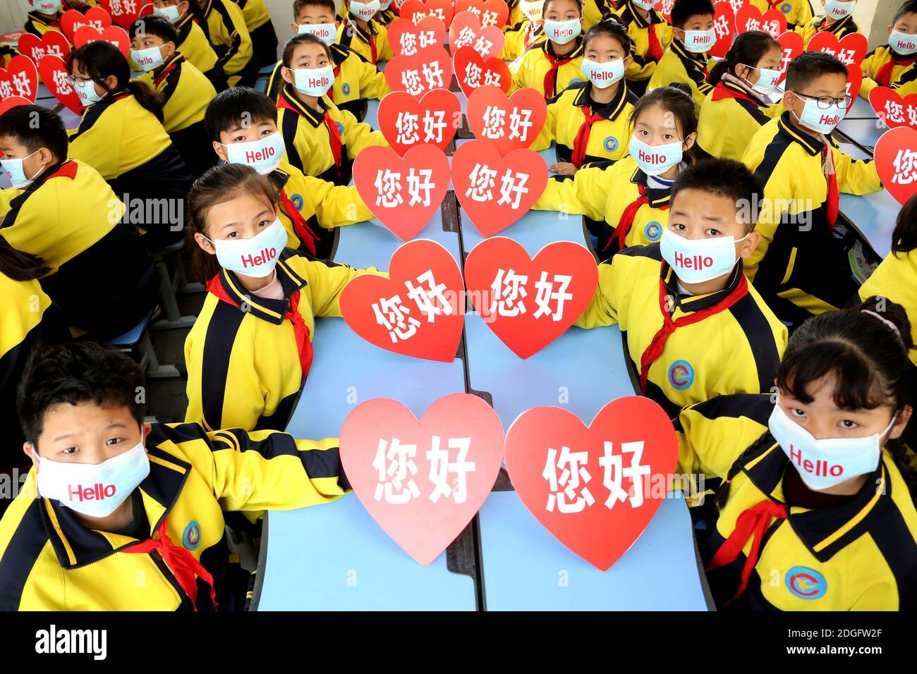 Pupils wear masks with Hello written on them and hold signs in their ...