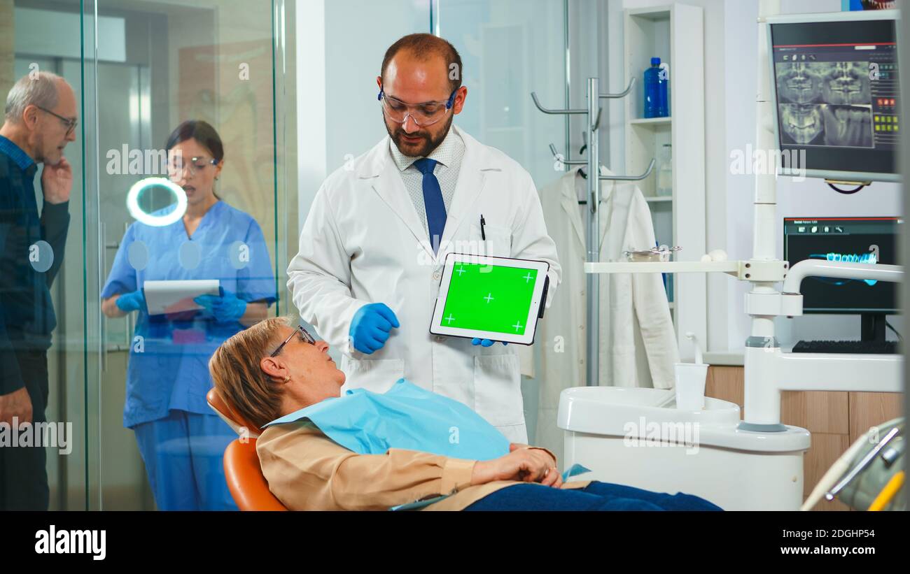 Dentist pointing at green screen display while patient lying on dental ...