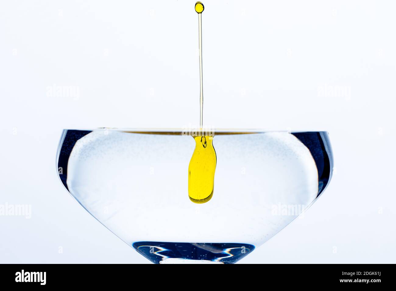Detail of dash of olive oil drops gliding into glass of water isolated ...