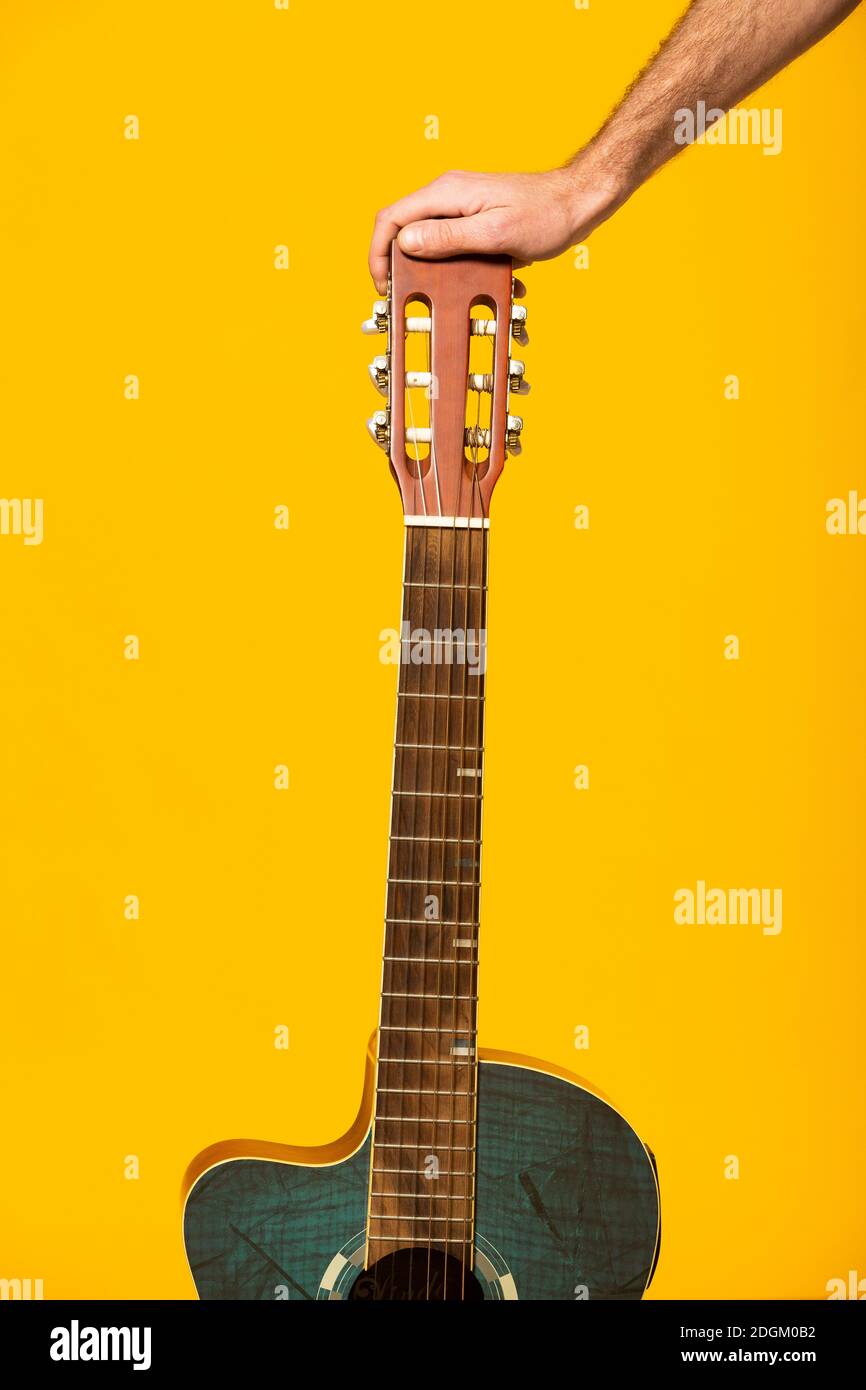 Human hand holding a blue acoustic guitar against a yellow background ...