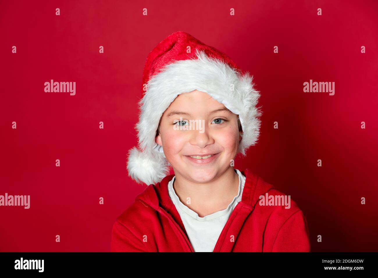 Pretty boy celebrating Christmas wearing Christmas hat in front of red ...