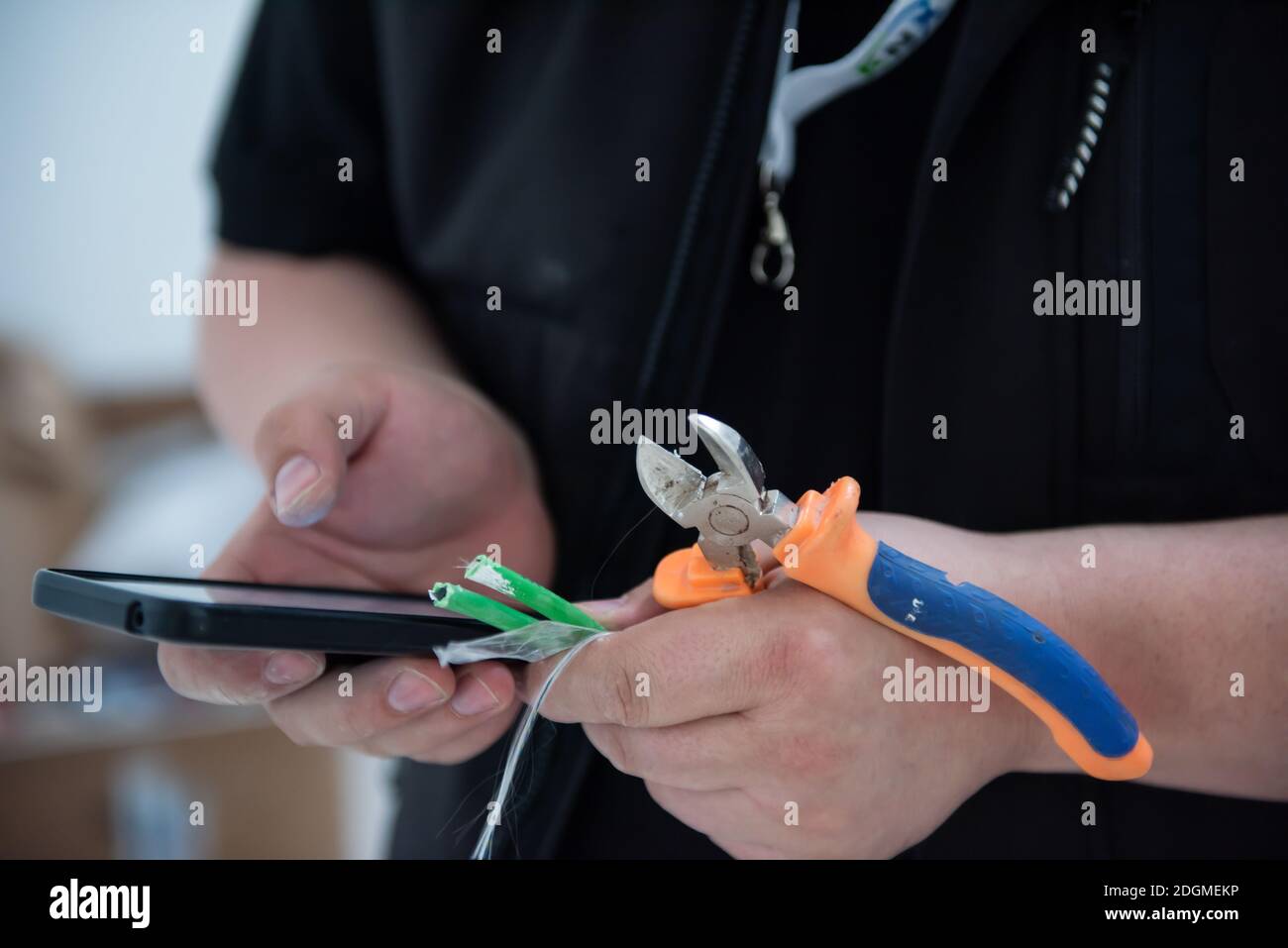 Electrical engineer with wire and pliers in his hand using mobile phone ...