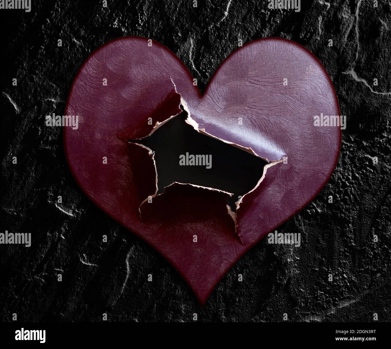 Hole ripped in heart shaped textured blue paper, on dark background ...