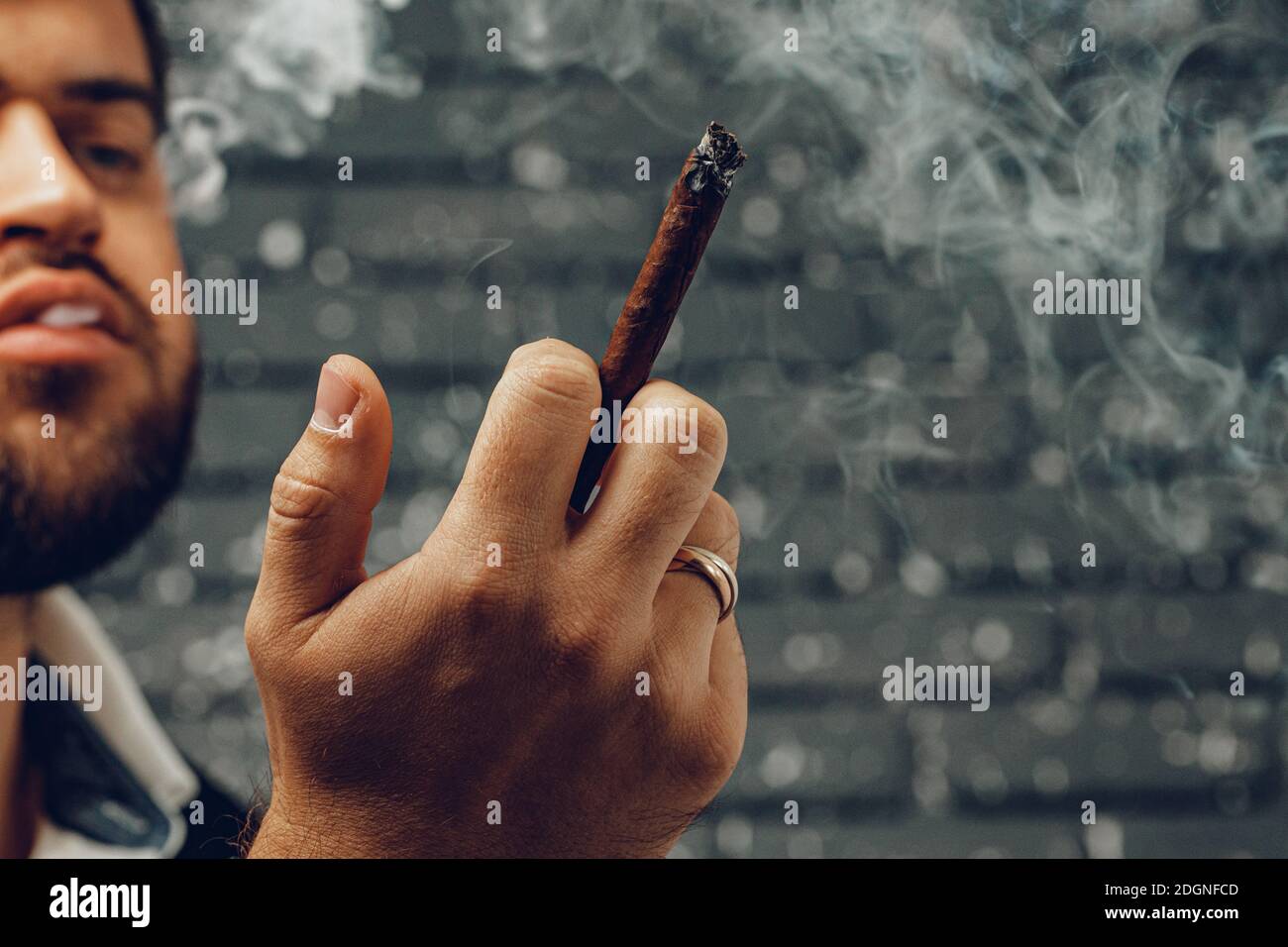 Bearded man smoking cigar against black brick wall Stock Photo - Alamy