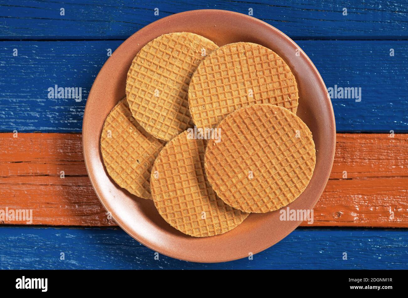 Round waffles with caramel in ceramic plate on colorful wooden surface ...