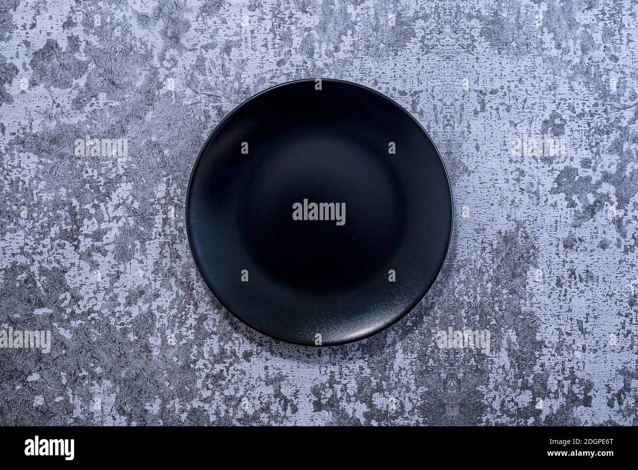 Black plate, cutlery on rustic stone table top view. Table setting ...