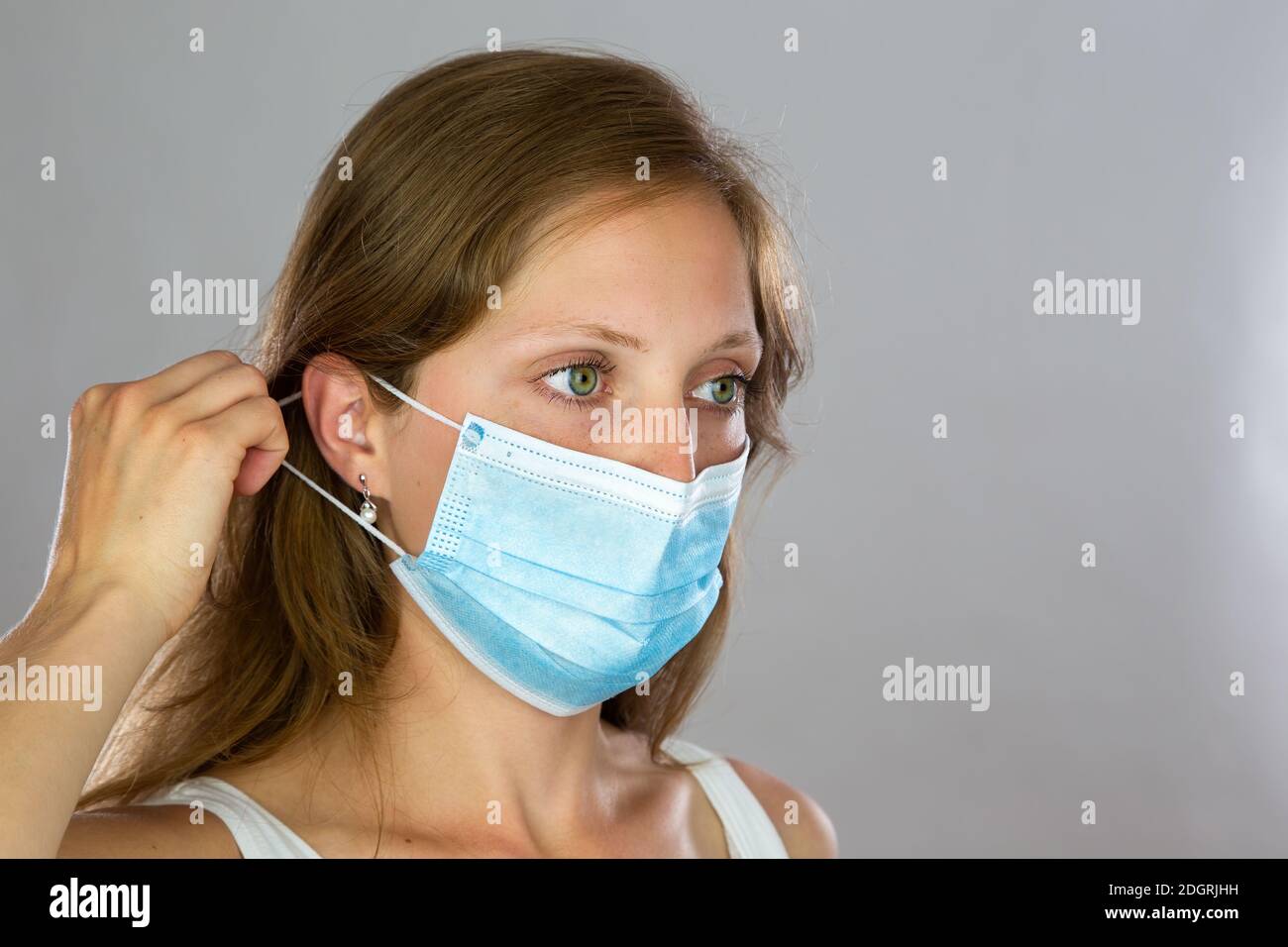 Female model in white shirt attaching surgical face mask on light ...