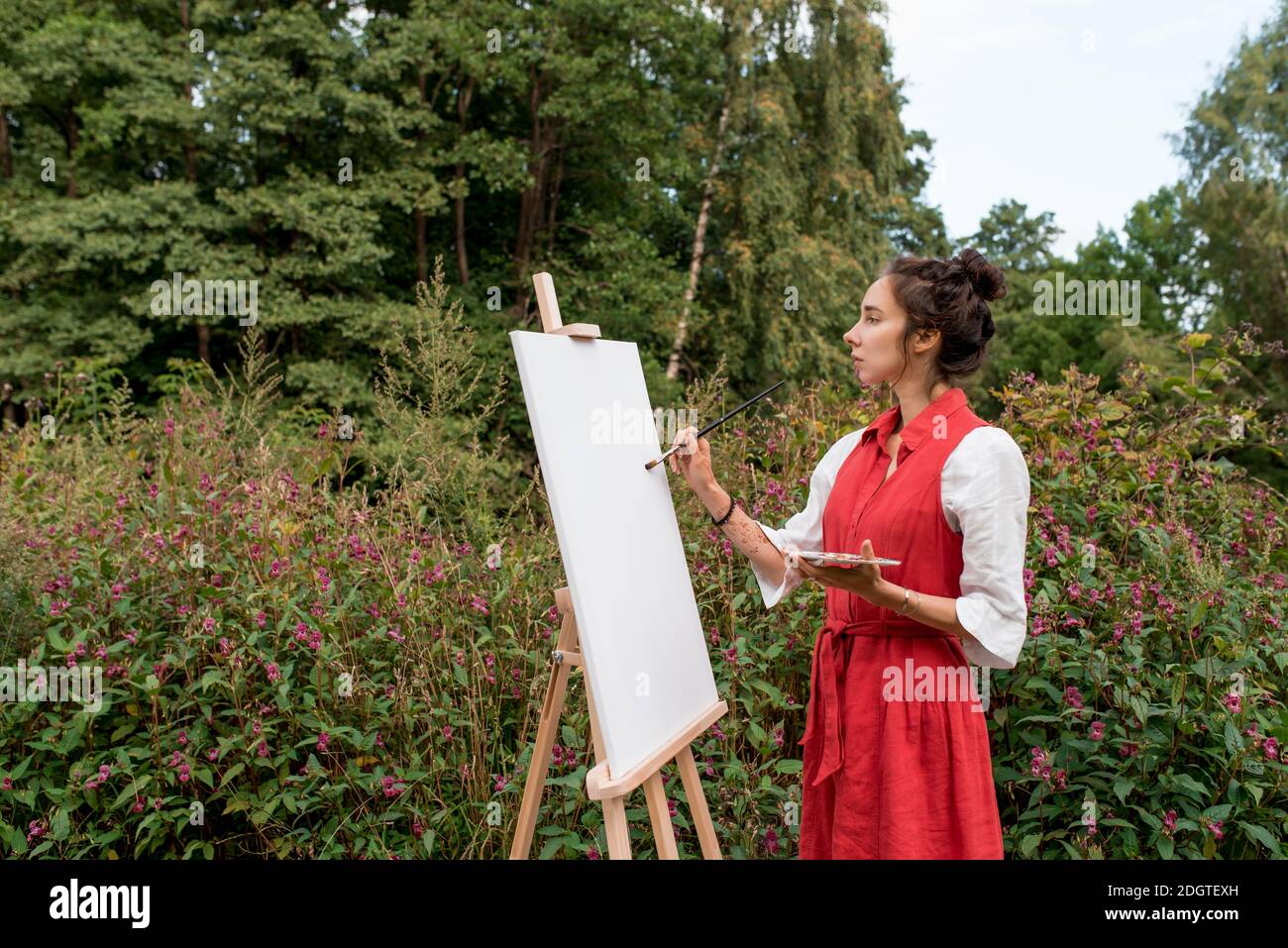 Getting started, woman in red dress, begins to paint picture, in summer ...