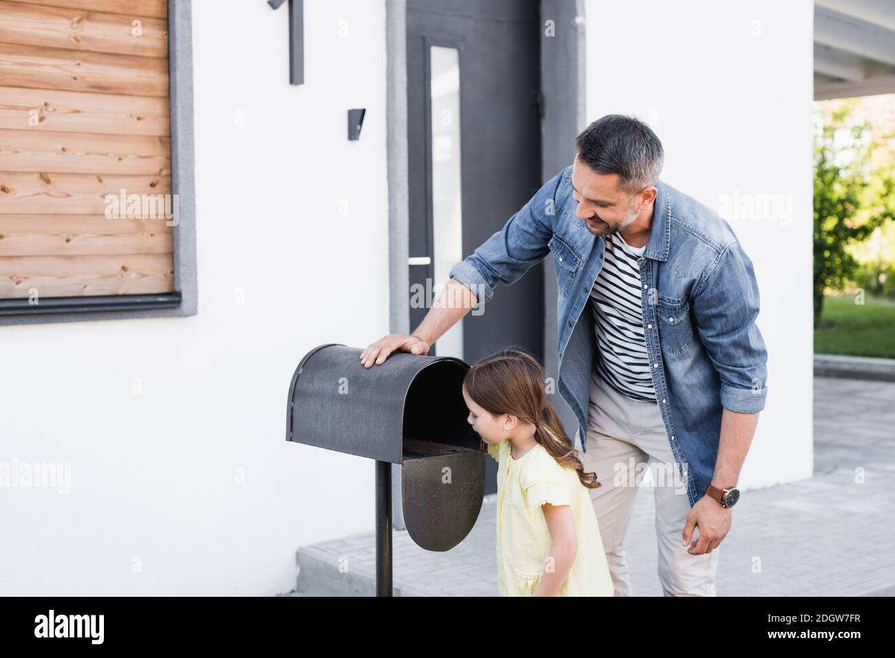 Smiling father standing near daughter looking in empty mailbox near ...