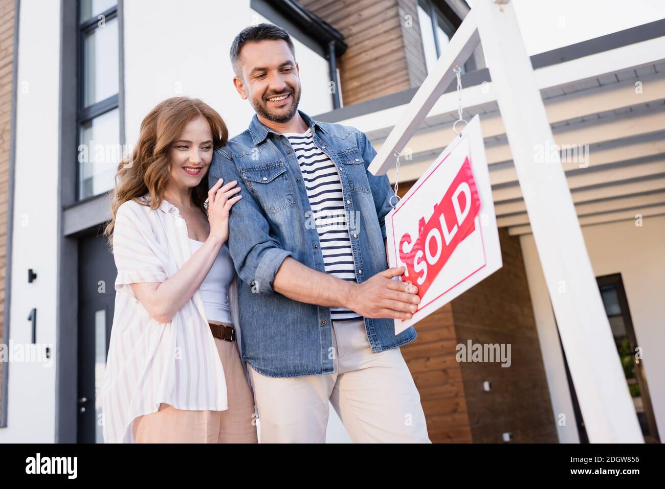 Cheerful couple looking at sign with sold lettering near house Stock ...