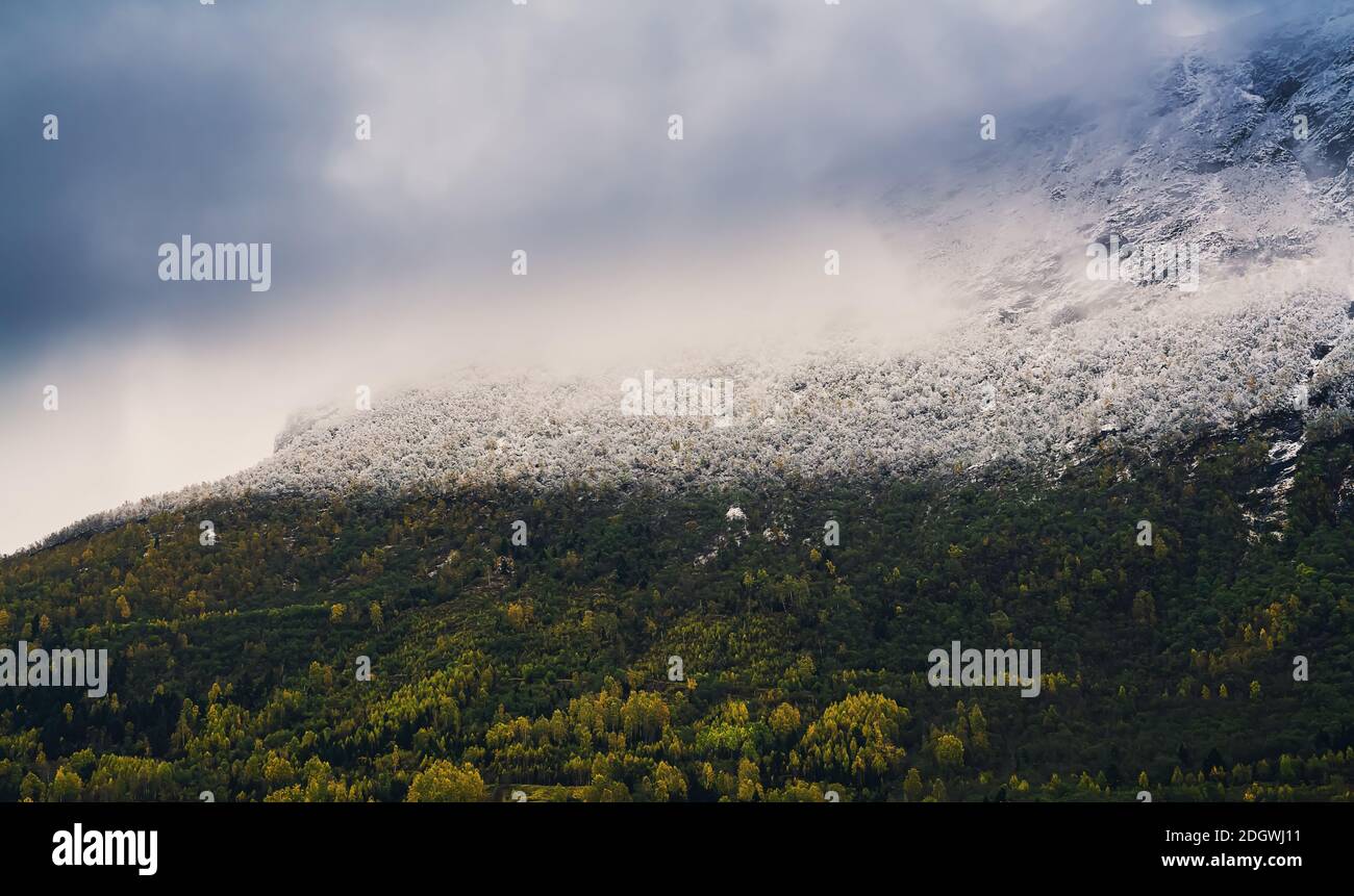 Mountain ridge with a clear snow line covered in dense stormy clouds ...