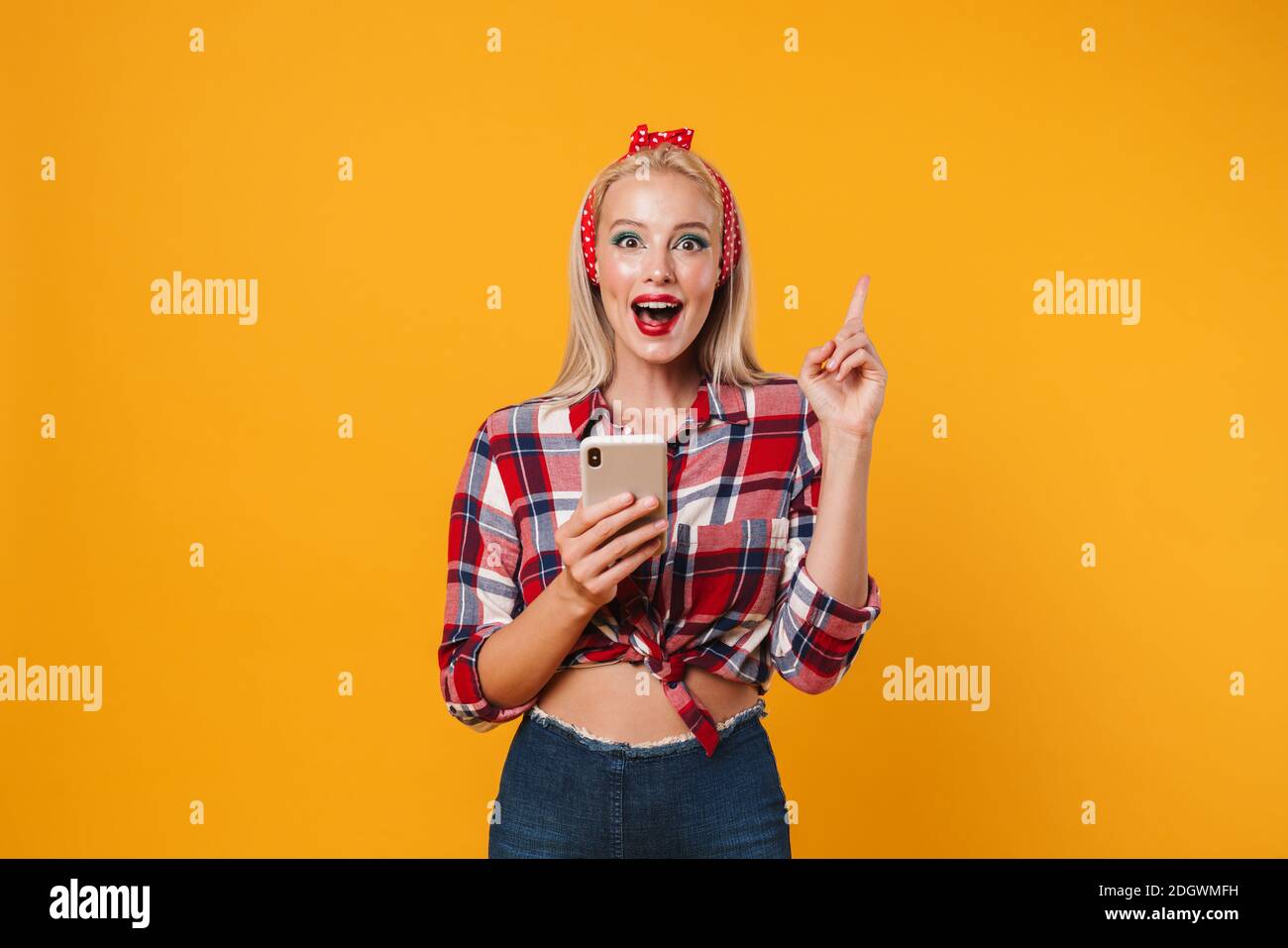 Image of surprised pinup girl pointing finger upward while using mobile ...