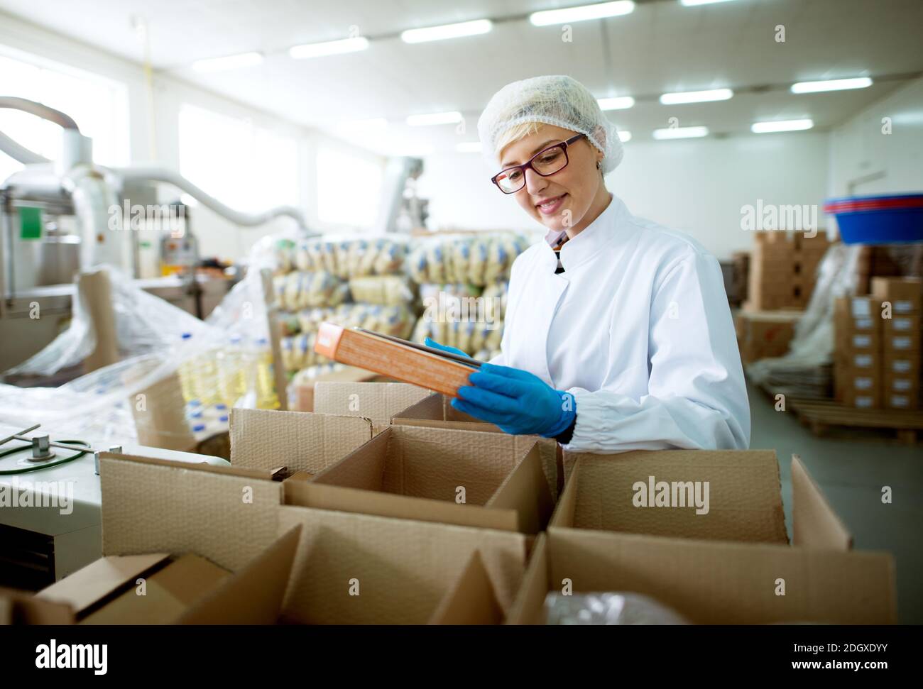 Young female dedicated worker is packing finished products in boxes in ...