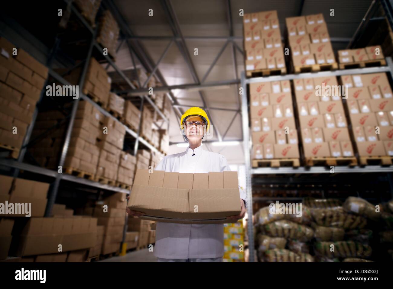 Young tensed hard working female worker is holding a big box stack near ...