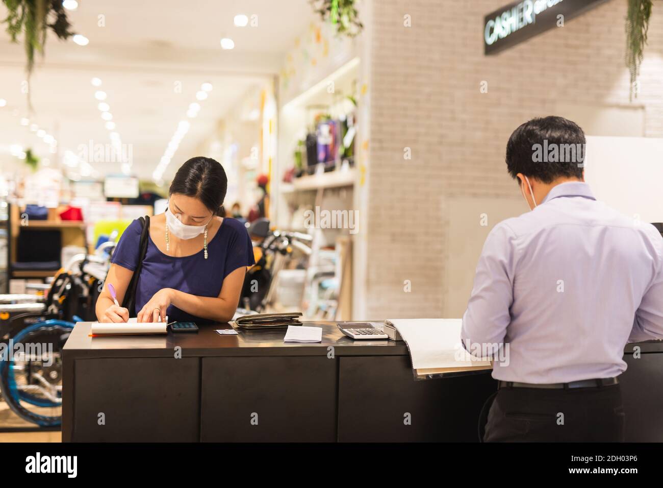 Woman in protective mask signing documents at cashier counter in ...