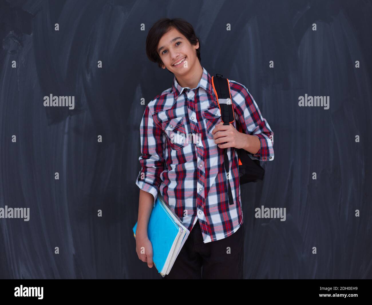 Arab teenager with school backpack and books against black chalkboard ...