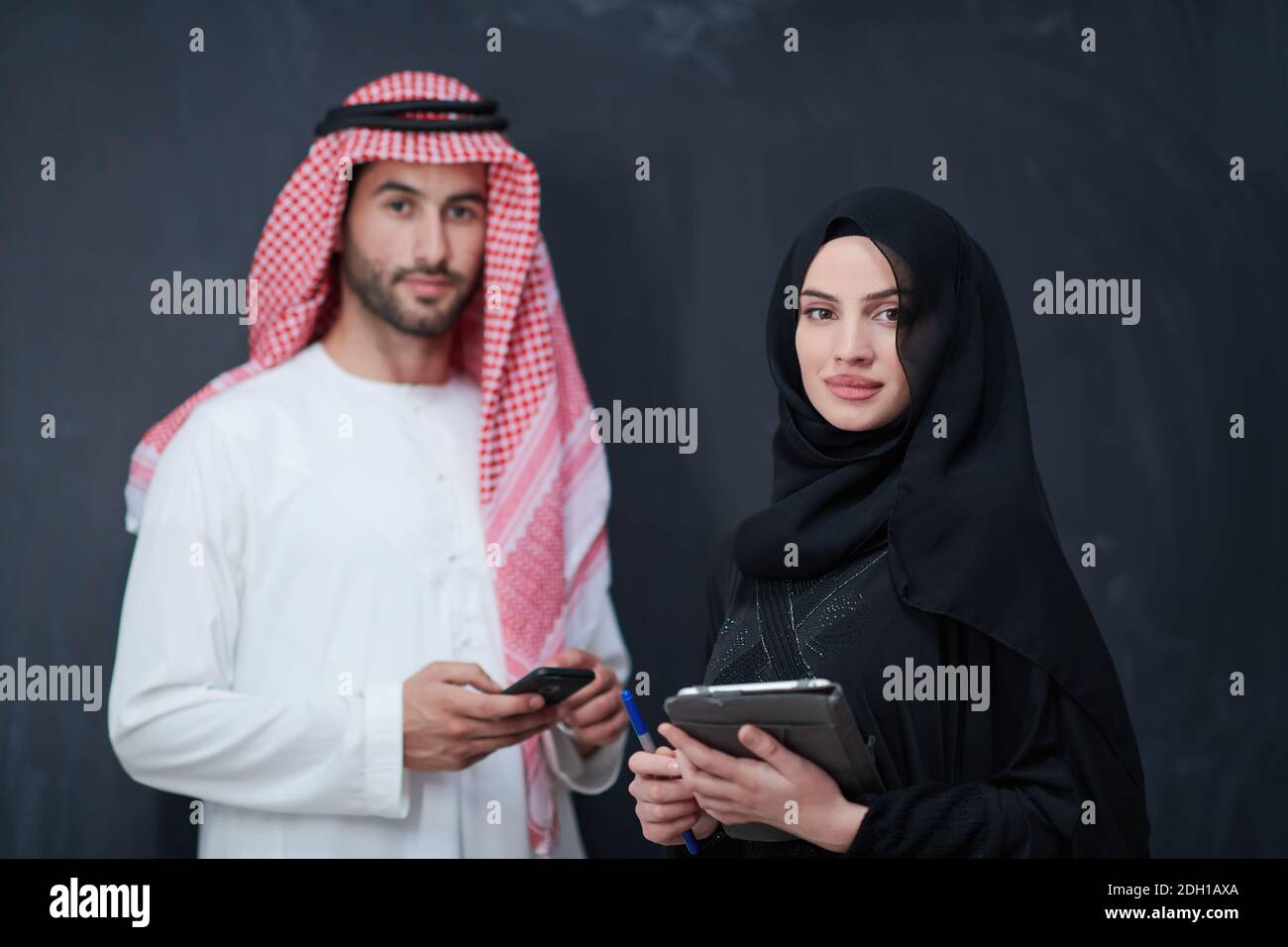 Muslim couple using modern technology in front of black chalkboard ...