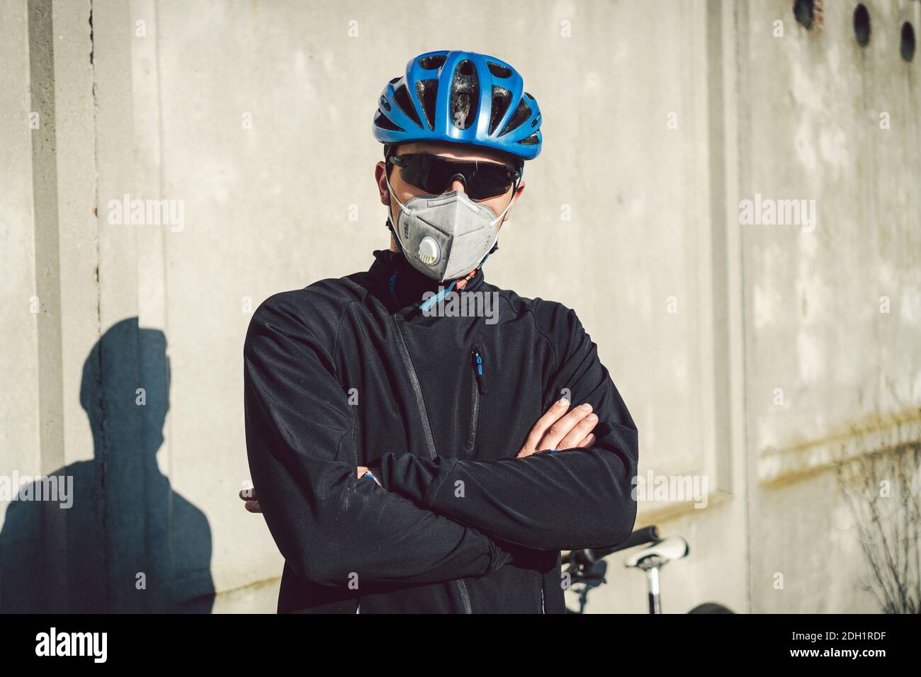 A man cyclist in a protective face mask stands next to a bicycle on a ...
