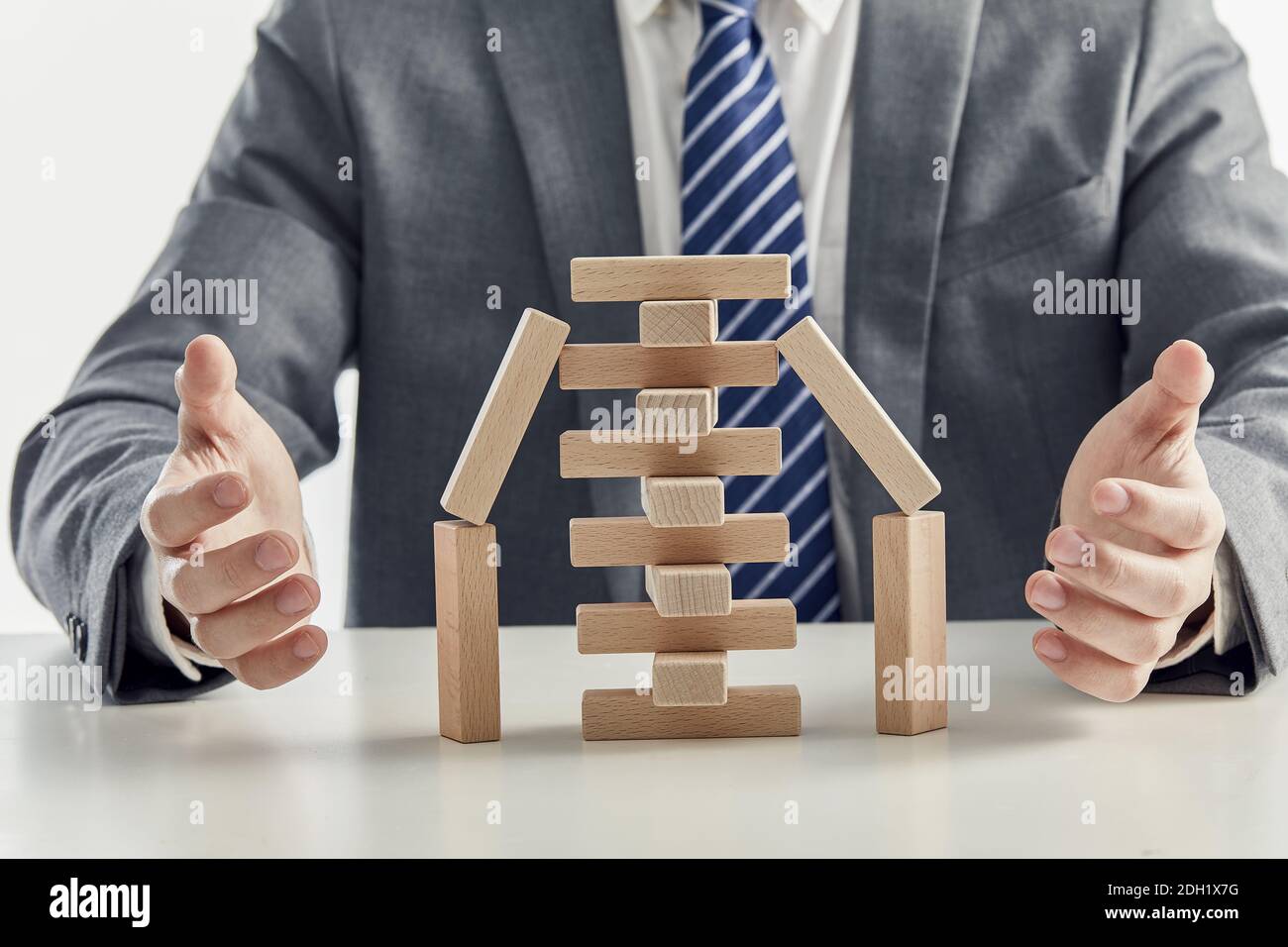 A businessman in a suit building an unusual tower using wooden blocks ...